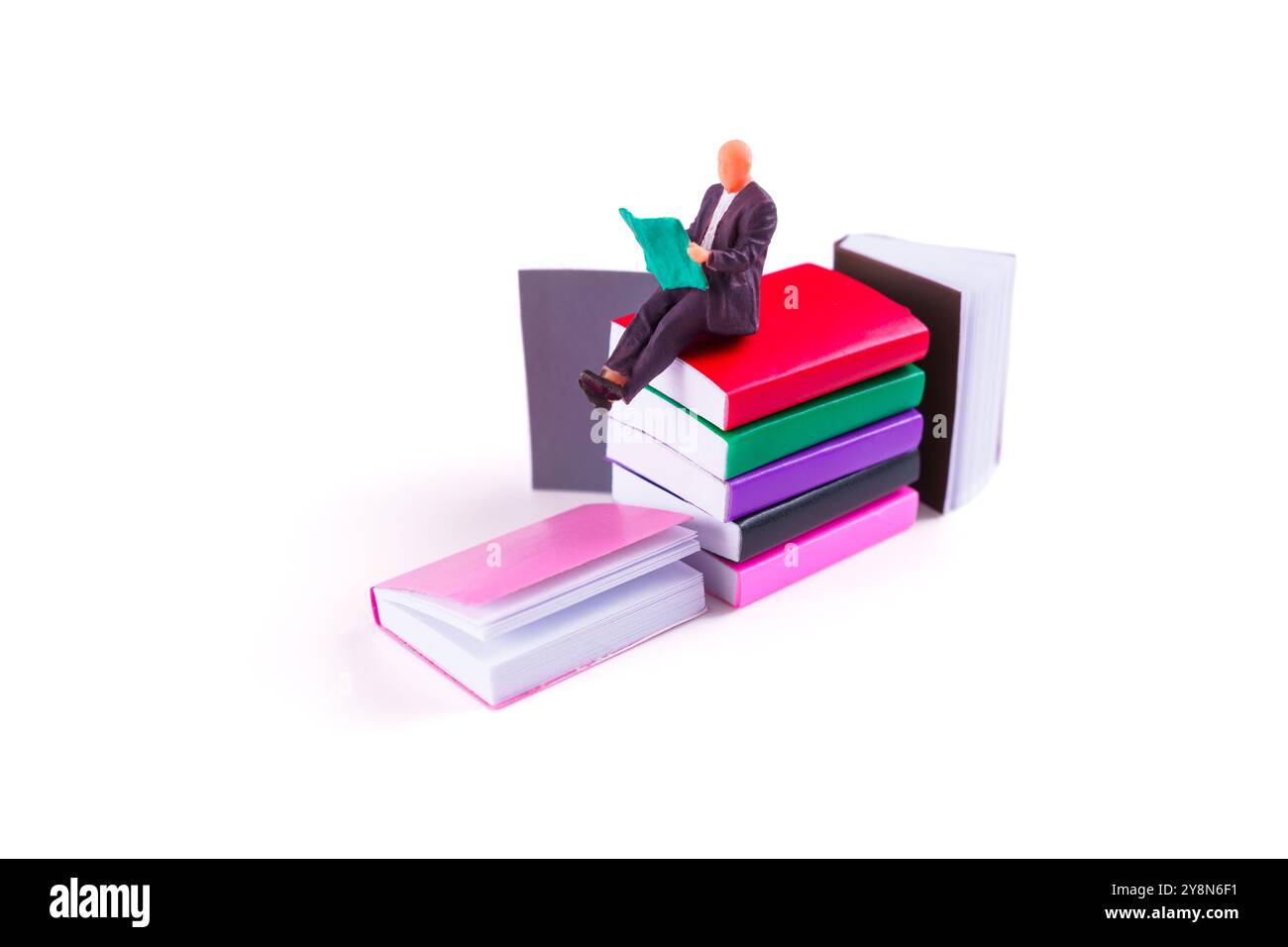 Small male figure in a suit reading a book while sitting on vibrant ...