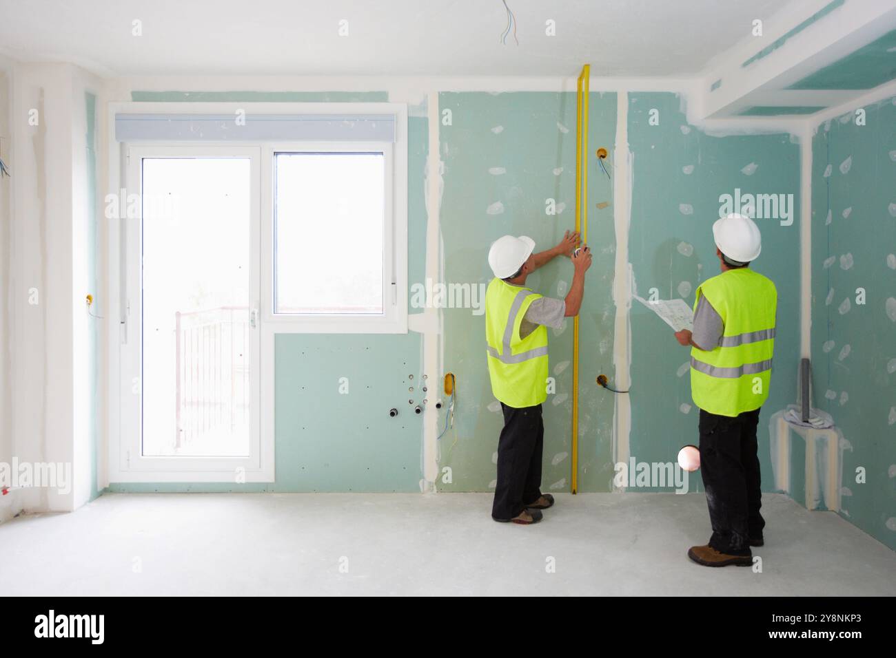 Workers with protective equipment, PPE, Measuring plasterboard panels ...