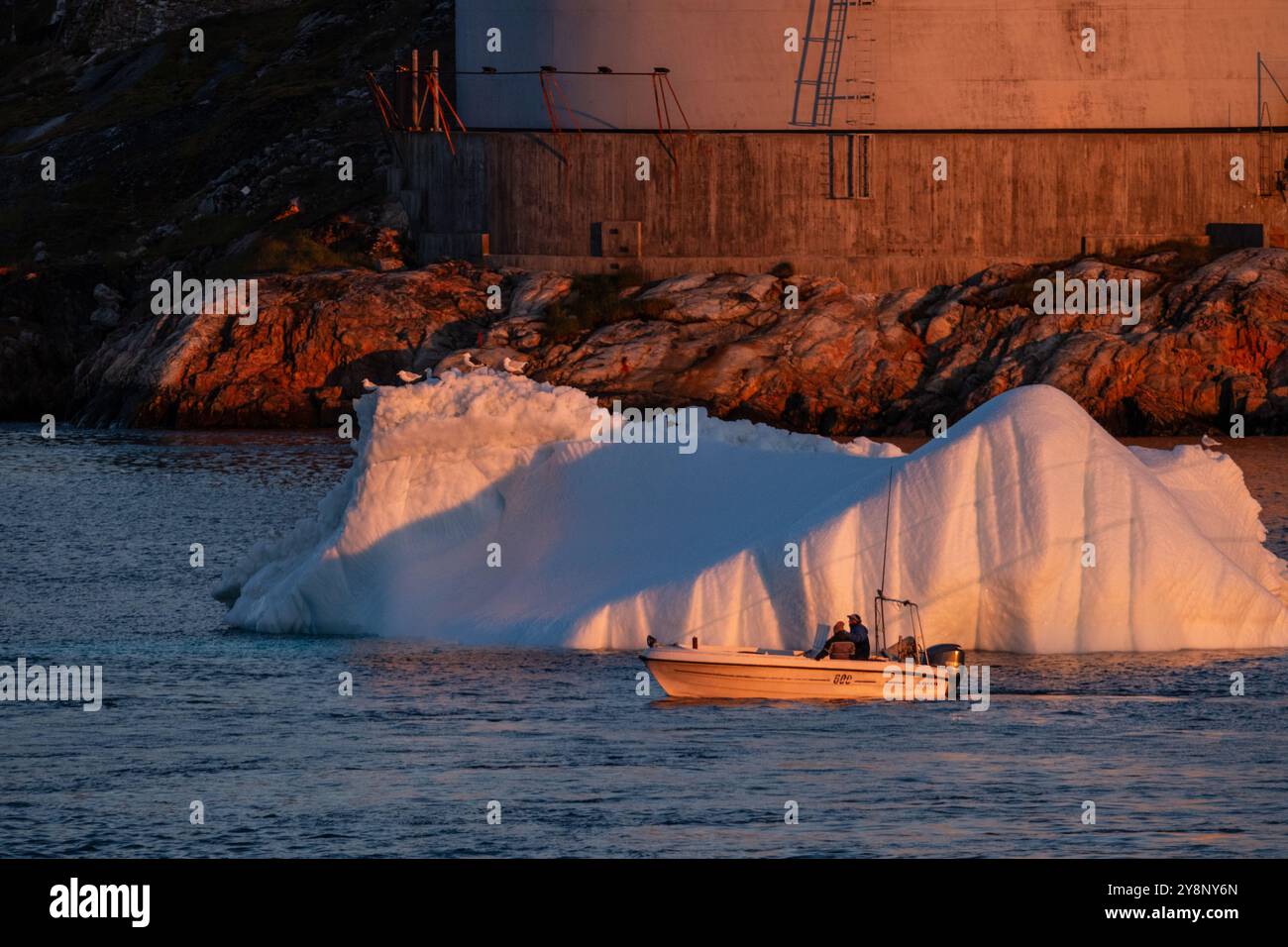 Small fishing boat sails past iceberg heading into port in small ...