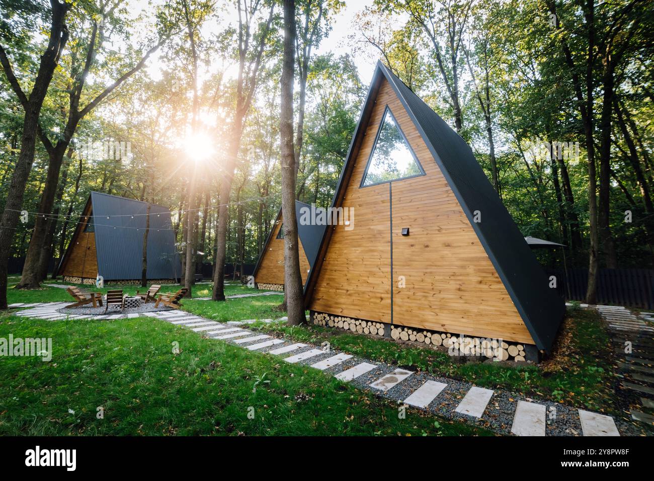 Cozy wooden A-frame cabins in forest with sunlight and outdoor seating ...