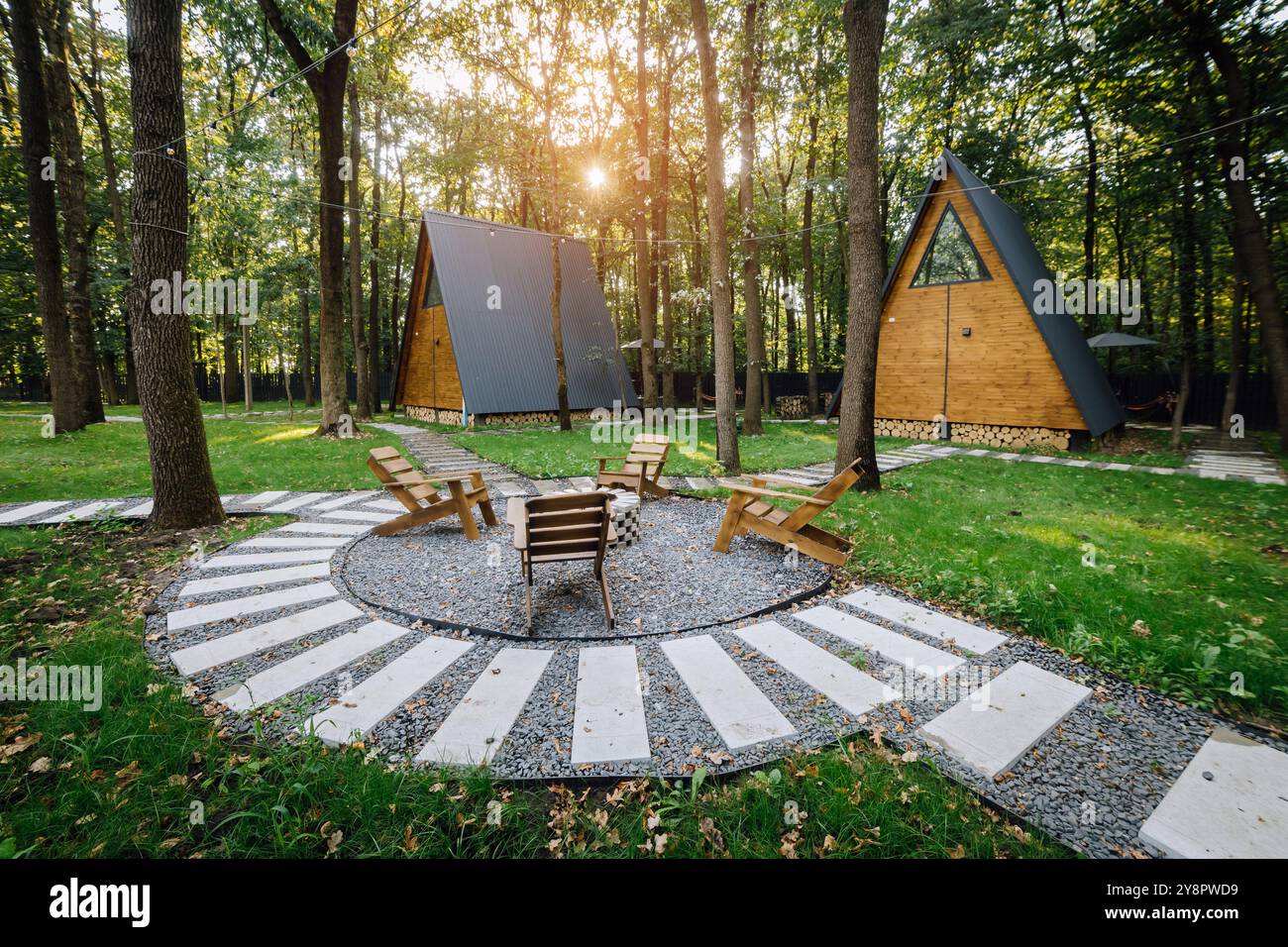 Modern wooden A-frame cabins in forest with outdoor seating and fire ...