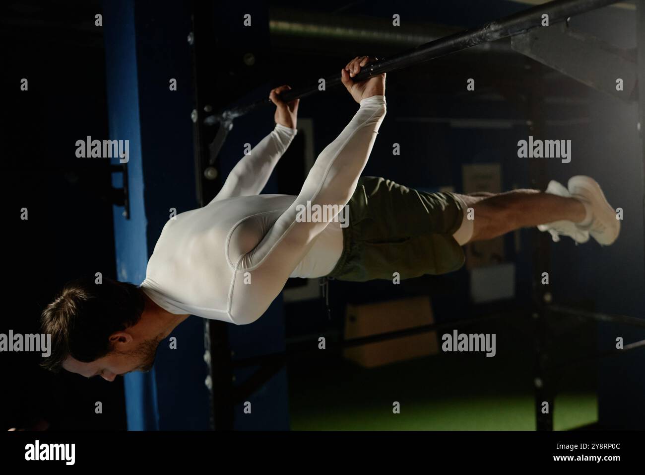 Fit sportsman performing back lever exercise with pronated grip holding ...