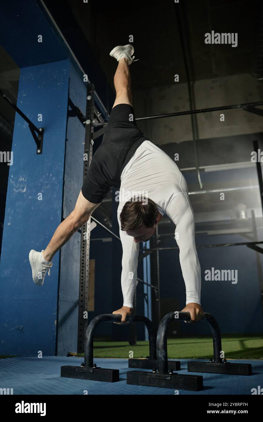 Vertical shot of muscular man in handstand position with one leg on ...