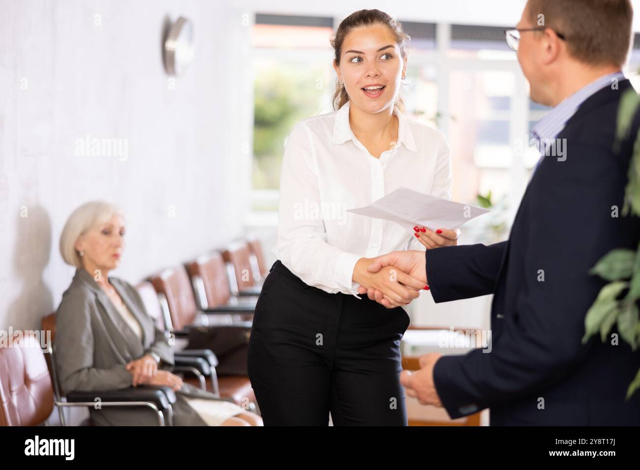 Young woman handshaking with other person in waiting room Stock Photo ...