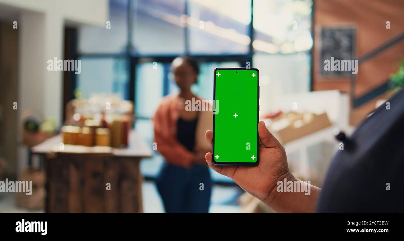 Retailer holding mobile phone with greenscreen layout, working at ...