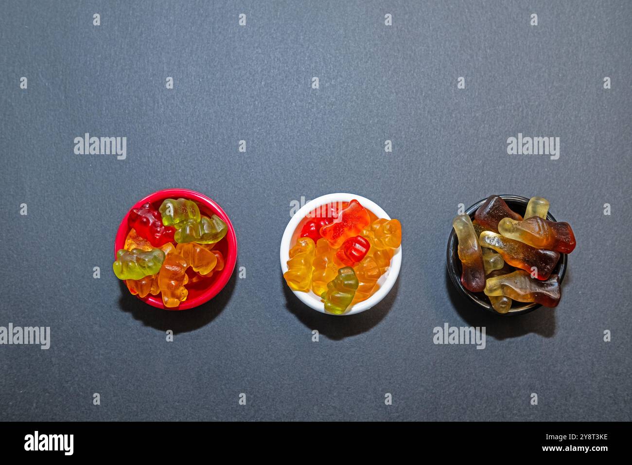 Colourful and small gel candies in small bowls. Grey ground and ...