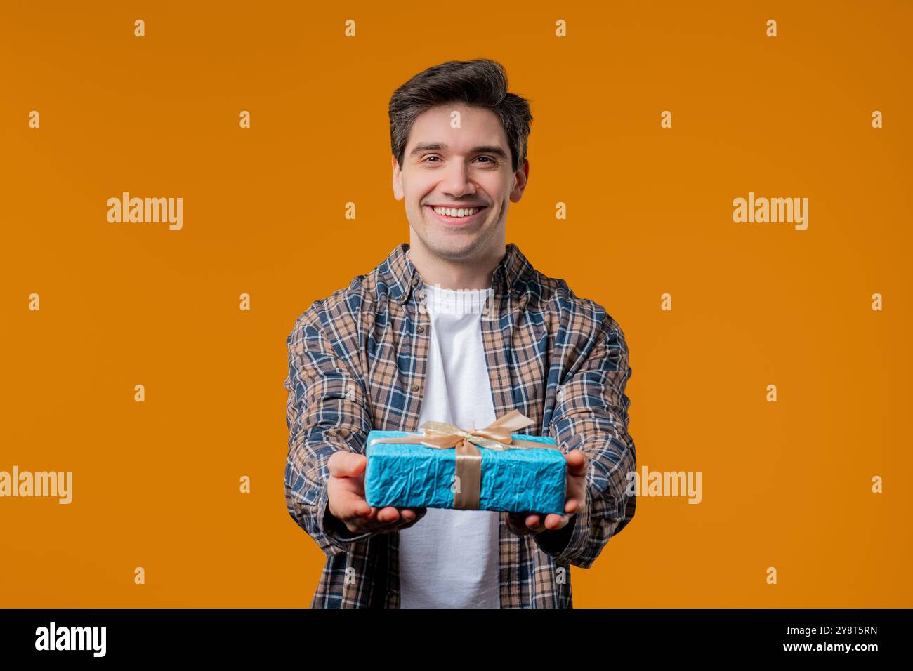 Man gives gift box by hands to camera on yellow background. Guy smiling ...