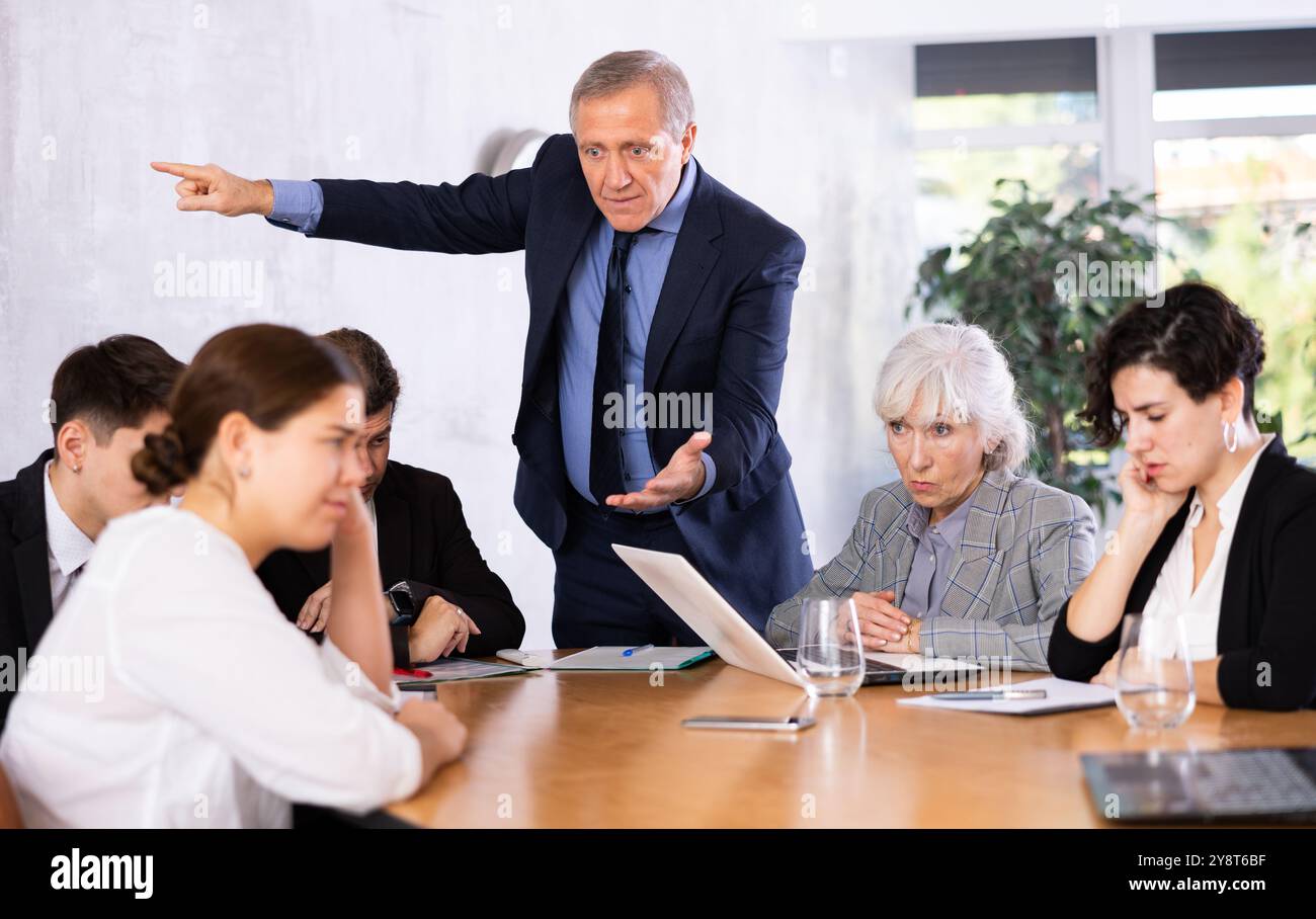 Annoyed senior male boss yelling at office colleagues of different ages ...
