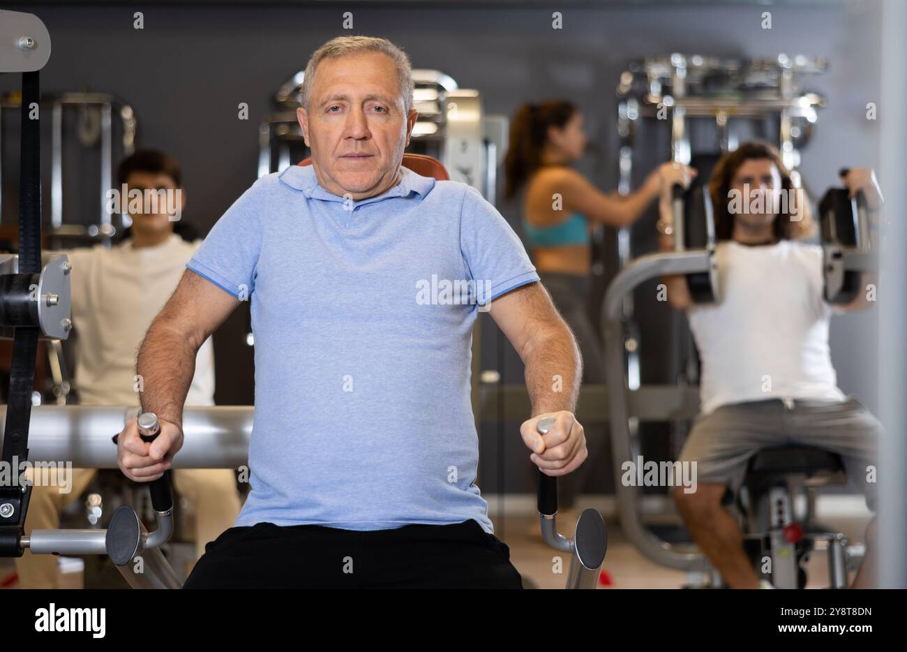Elderly active man exercising on a simulator in modern gym Stock Photo ...