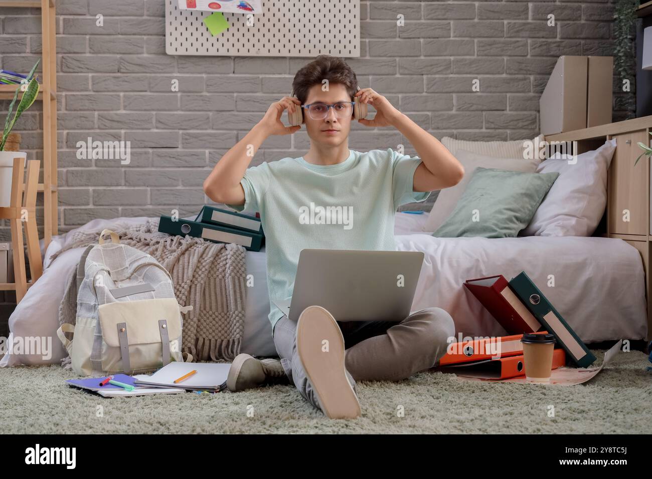 Male medical intern with headphones and laptop studying in bedroom ...