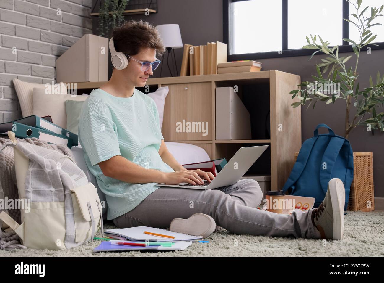 Male medical intern with headphones and laptop studying in bedroom ...