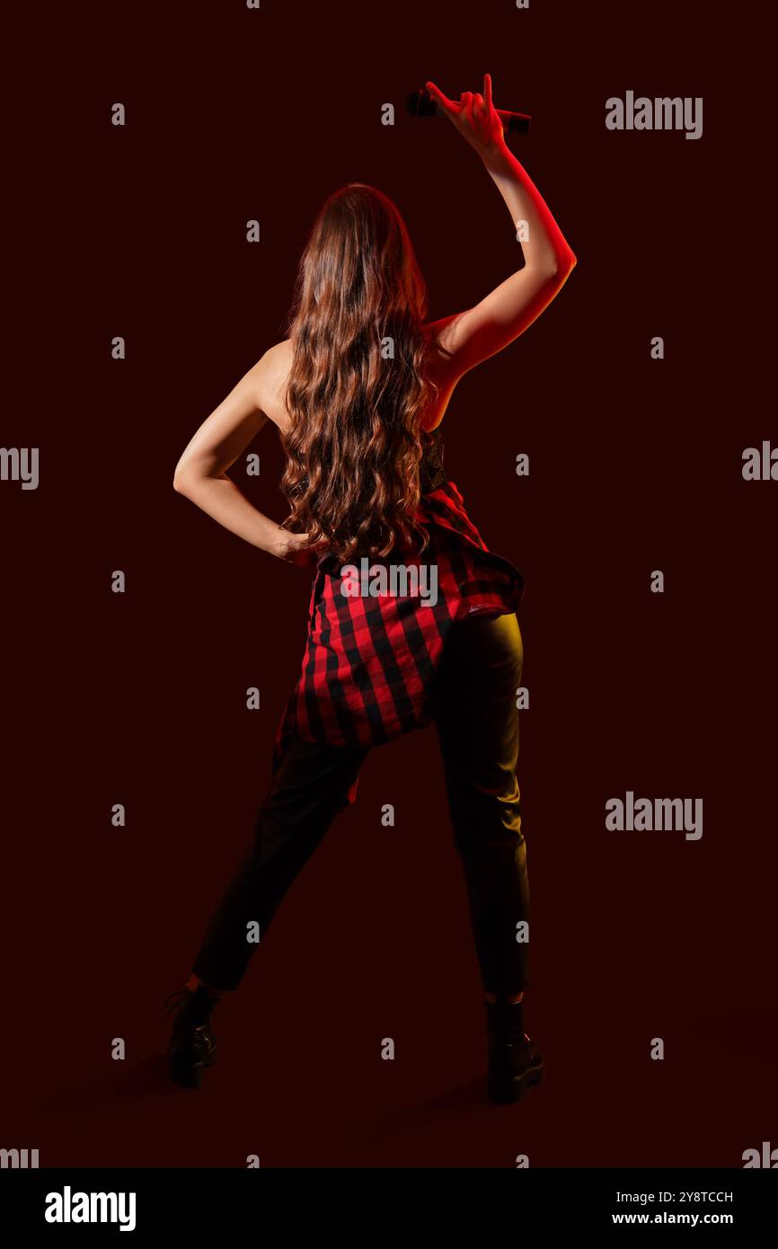 Female singer with microphone showing "devil horns" on dark red ...
