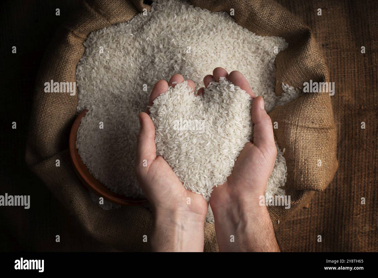 Human hands in shape of heart holding handful of rice over burlap sack ...