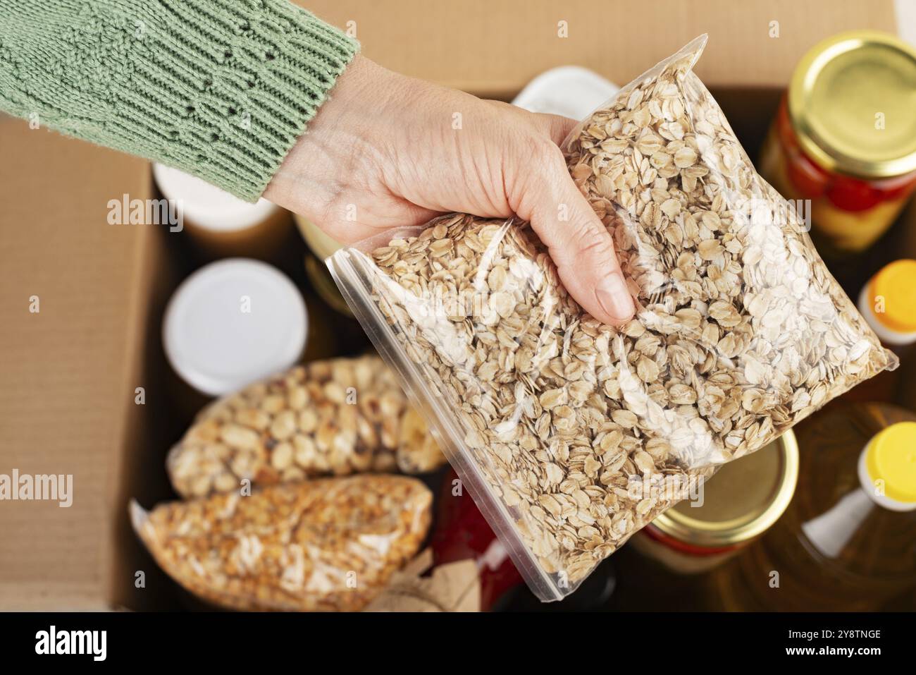 Plastic container with rolled oats in female hand on emergency food box ...