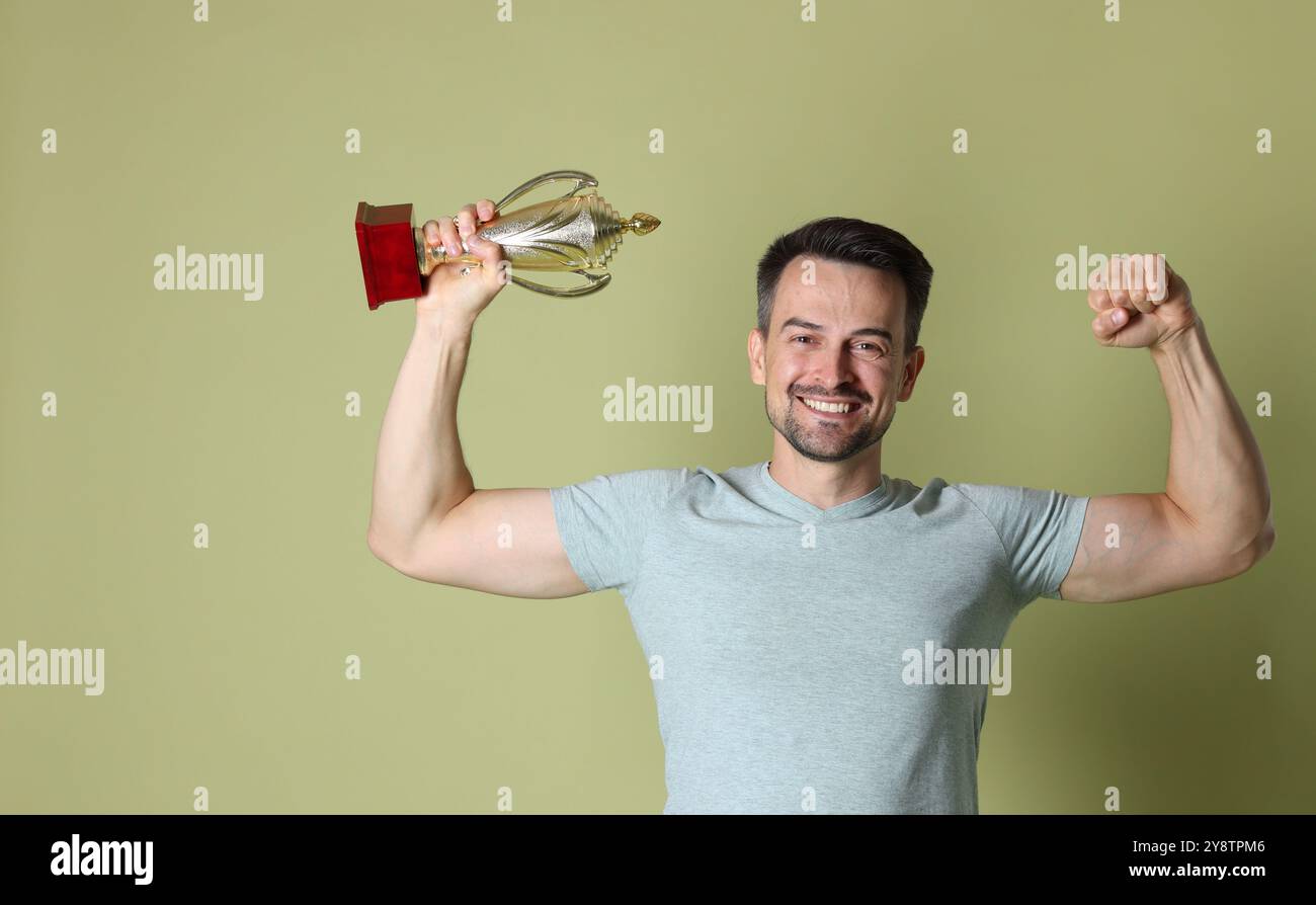 Happy winner with golden trophy cup showing his biceps on pale olive ...