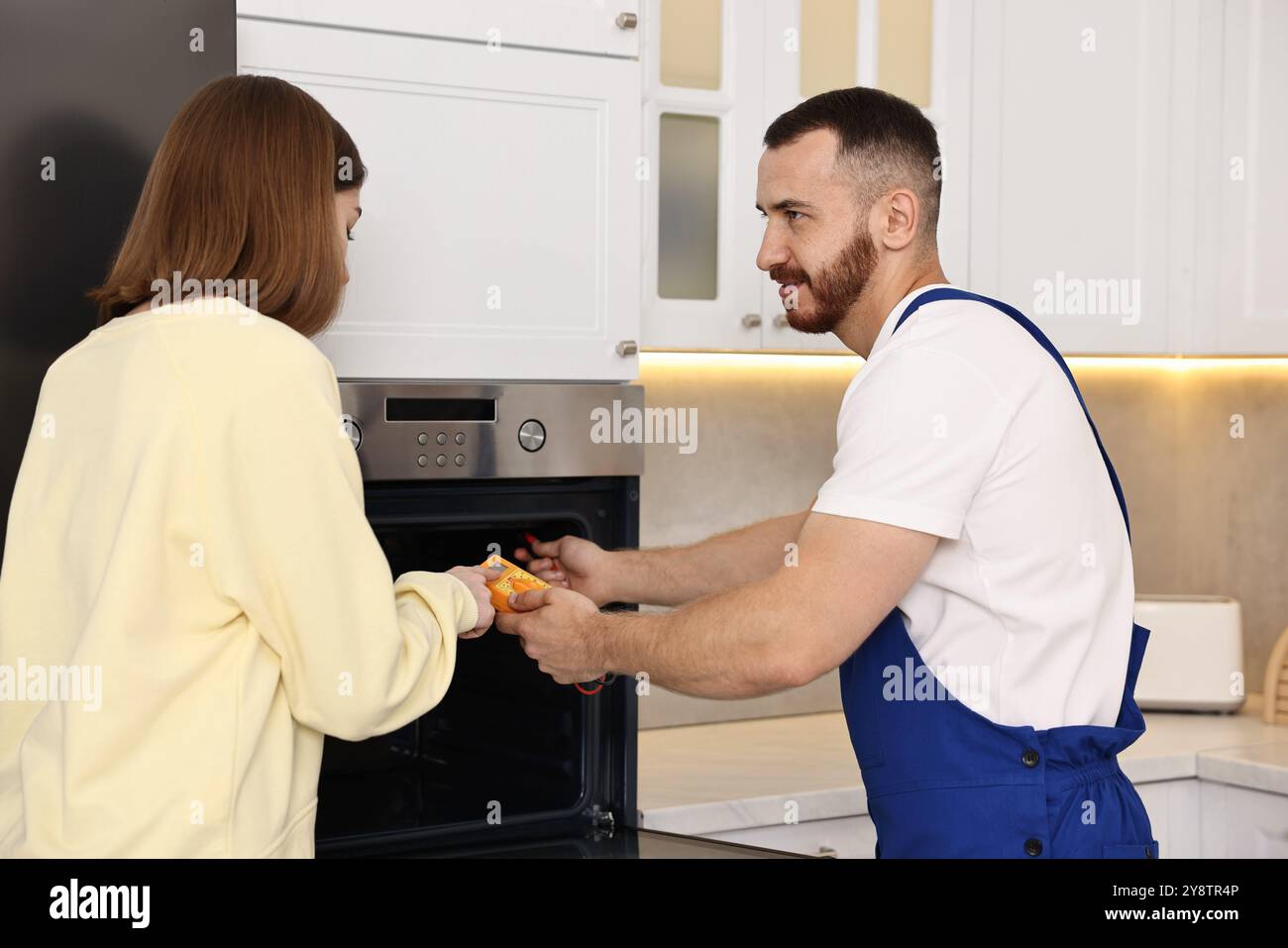 Repairman showing woman how to use multimeter near oven in kitchen ...