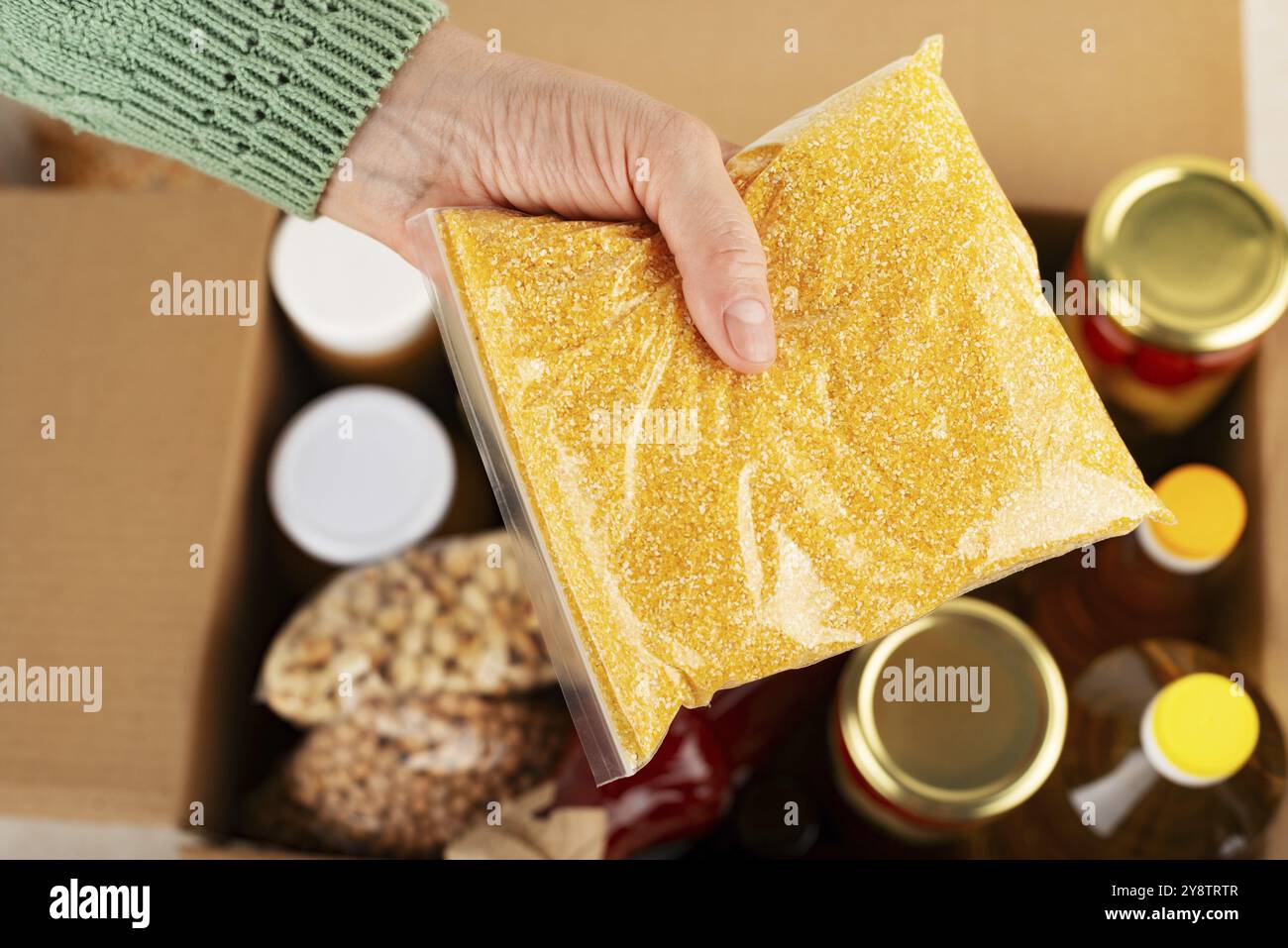 Plastic container with corn grits in female hand on emergency food box ...