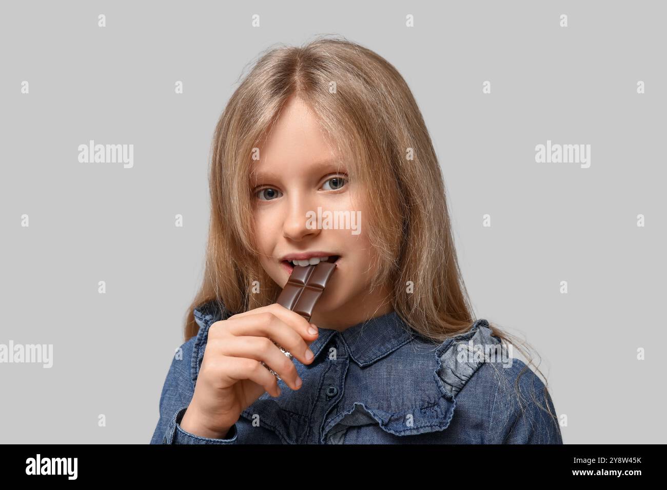 Cute little girl eating sweet chocolate on grey background Stock Photo ...