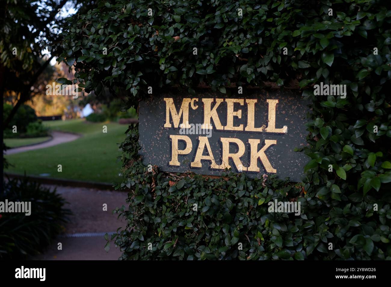 Gold leaf wall plaque McKell Park nestled in green ivy with a view of the park beyond, at ...