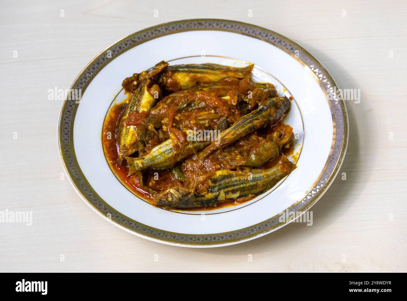 Tasty tengra fish cooked and served in a white plate, placed on a light ...
