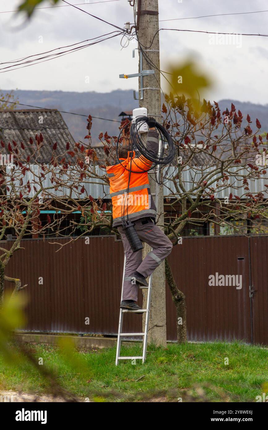 A technician climbs a ladder with wires in his hands to connect a fiber ...
