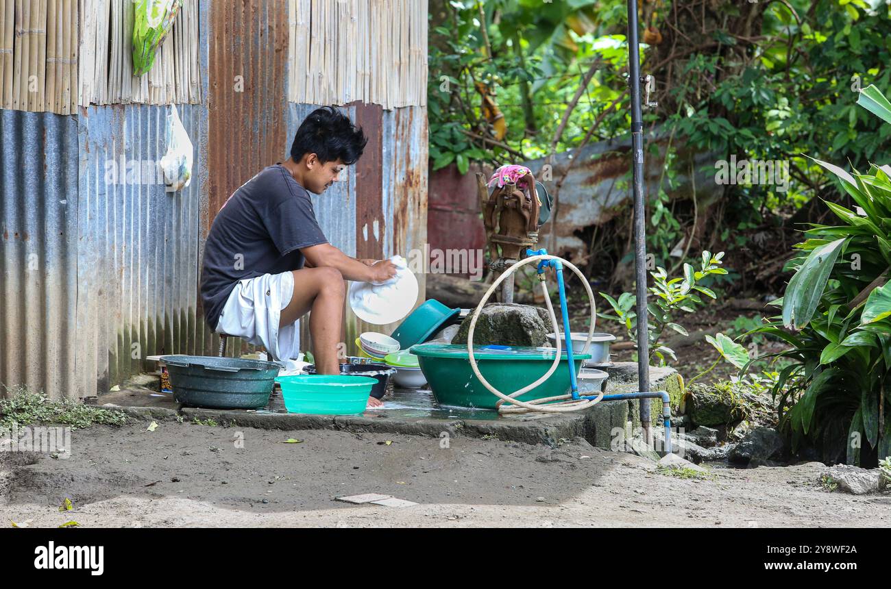 Philippines : A Filipino man washing the dishes in his house backyard ...