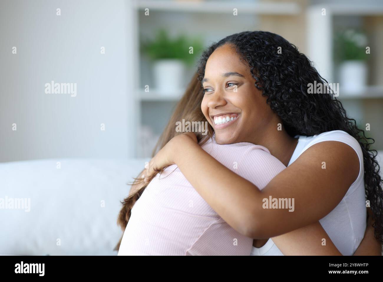 Happy black woman hugging her friend on a couch at home Stock Photo - Alamy