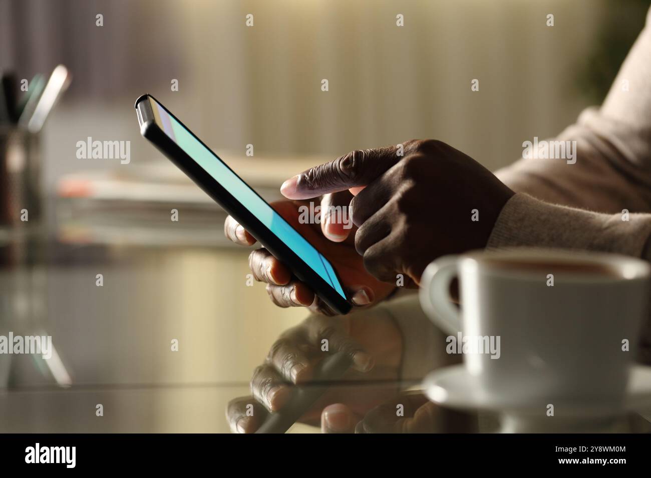 Close up of a black man hand using mobile phone on a desk in the night ...