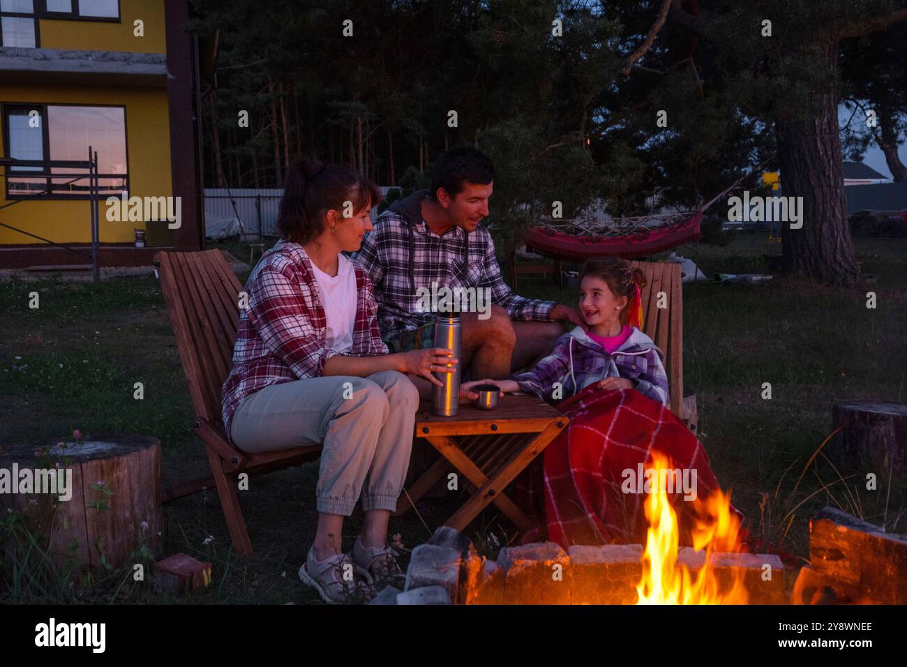 Family is sitting by the outdoor campfire in the courtyard of the house ...