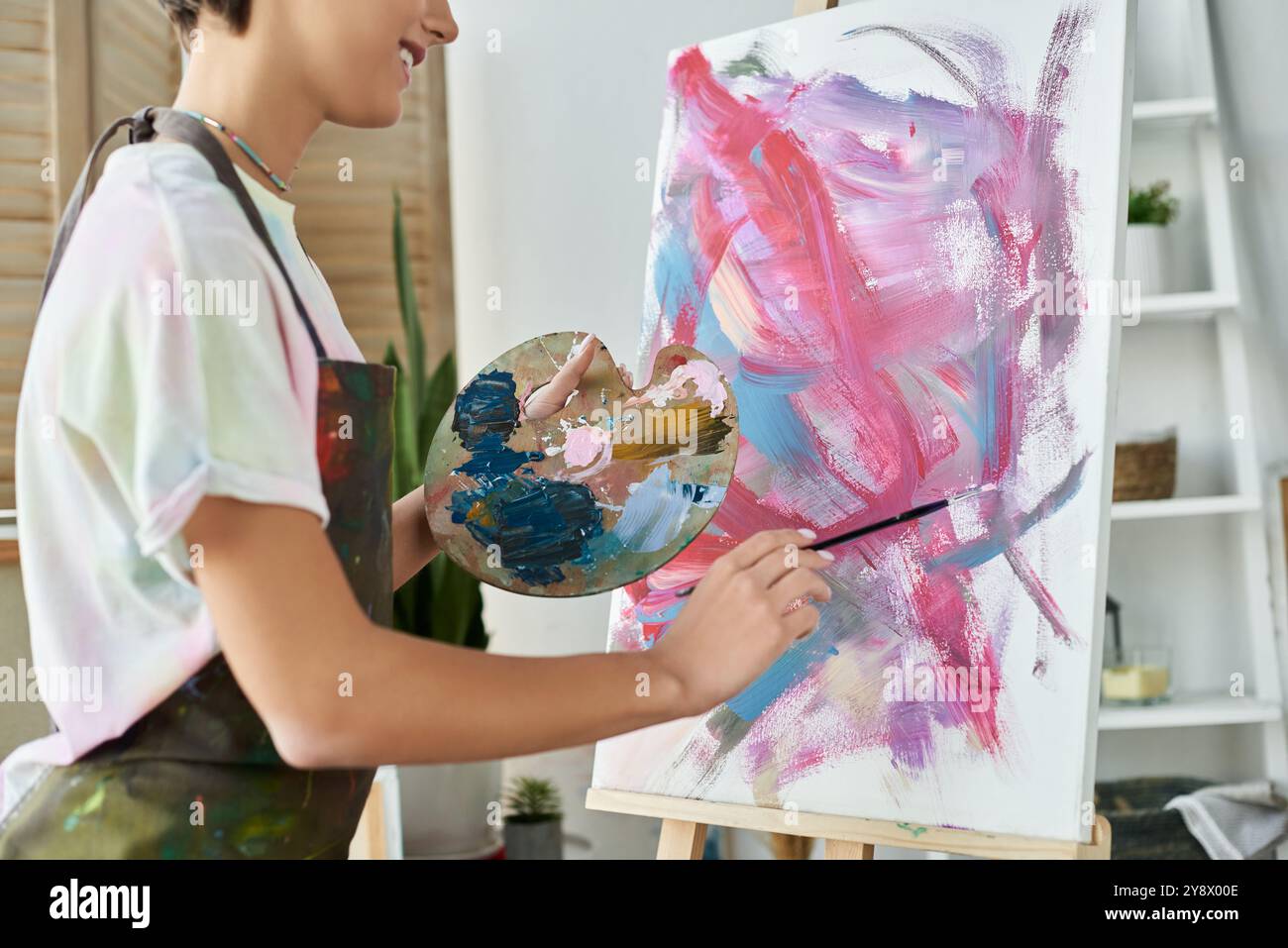 A young woman with short hair joyfully creates an abstract painting in ...