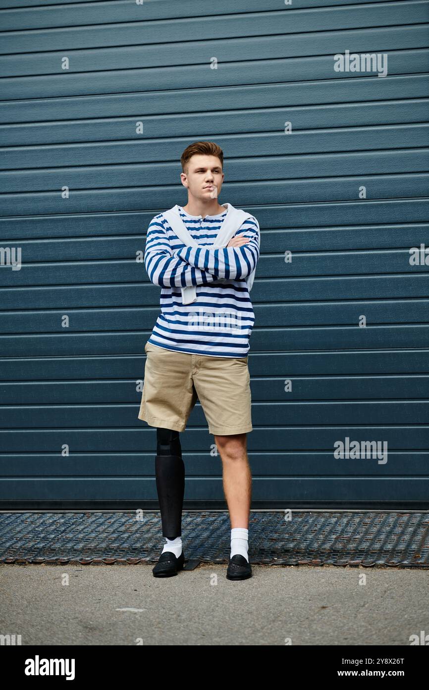 A young man with crossed arms showcases his prosthetic leg against a ...