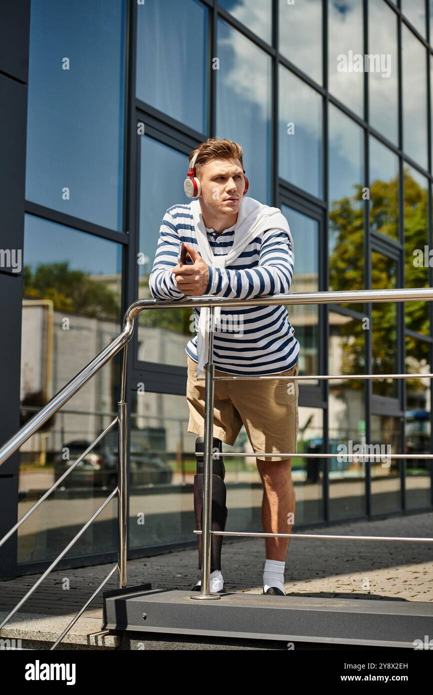 A young man leans casually on a railing, listening to music while ...