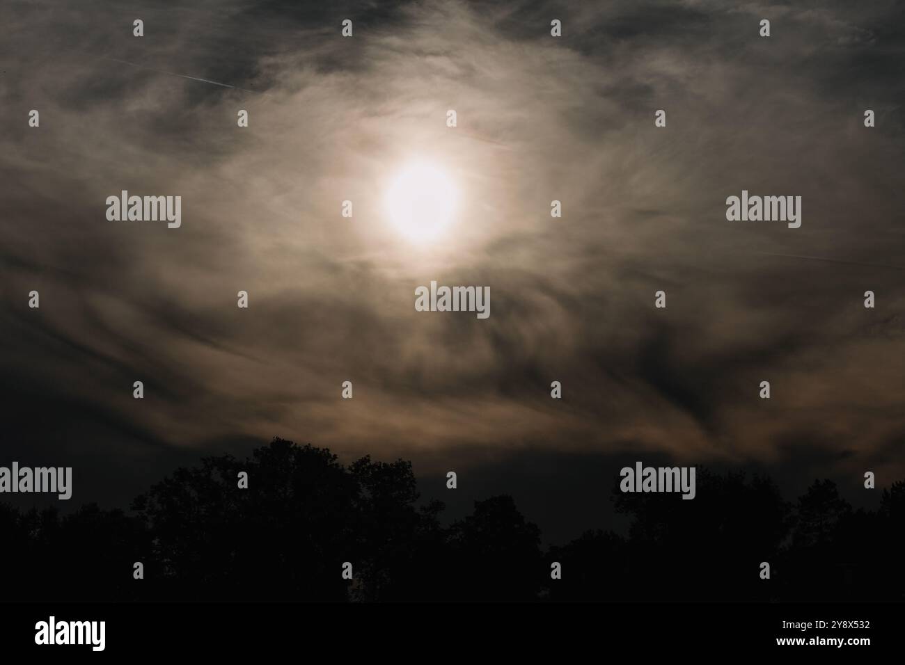 A soft focus image of the sun partially obscured by thick clouds ...