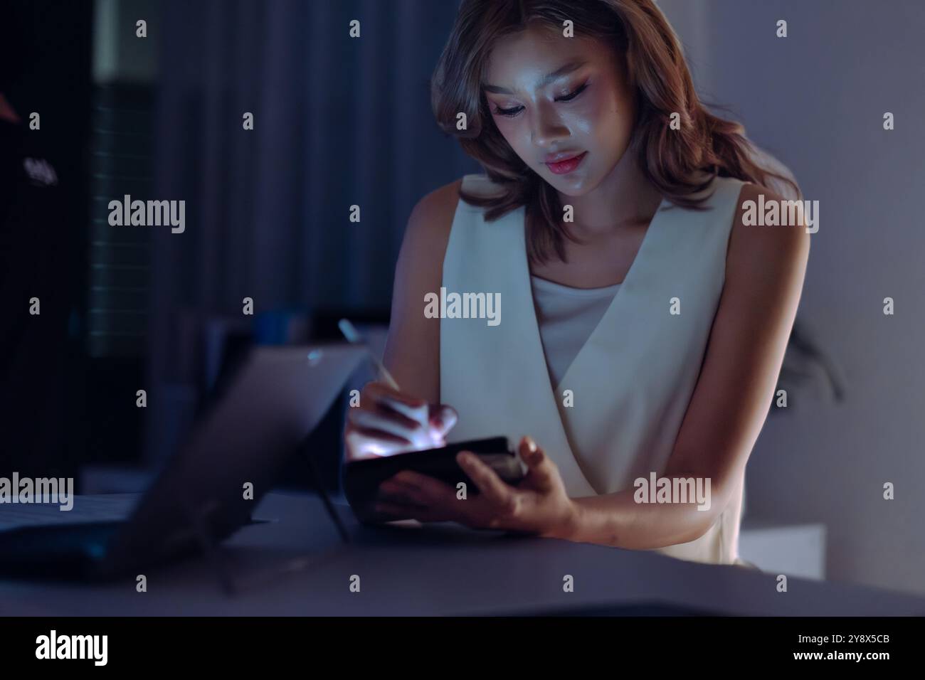 asian business woman use digital tablet working in a dimly lit office, analyzing financial ...