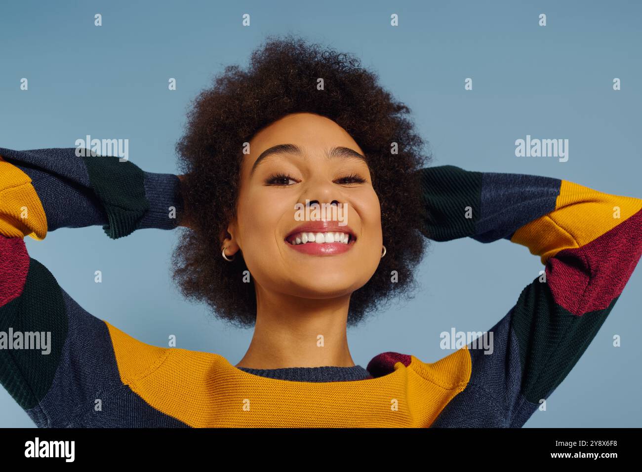 A young woman beams with joy, her hands behind her head, radiating ...