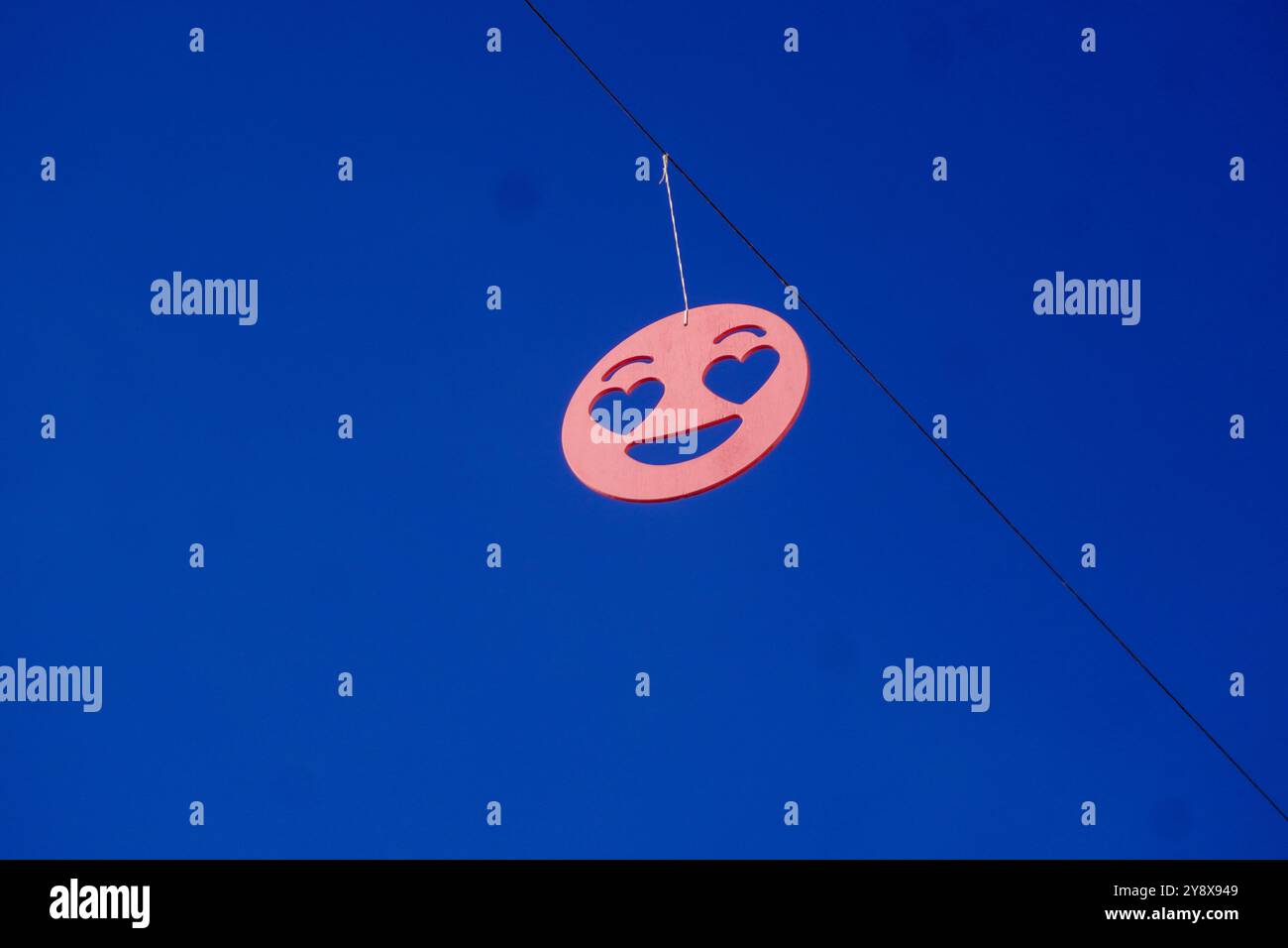 Two suspended objects , a smiling orange emoji against a clear blue sky ...