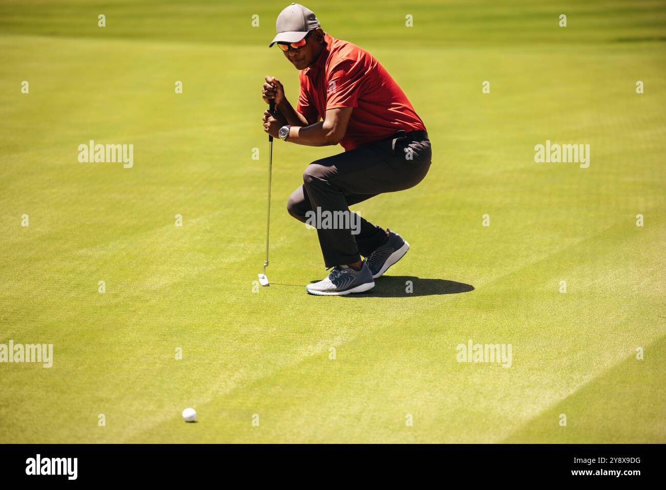 Male golfer leaning on a putter on the green, focusing intently on ...