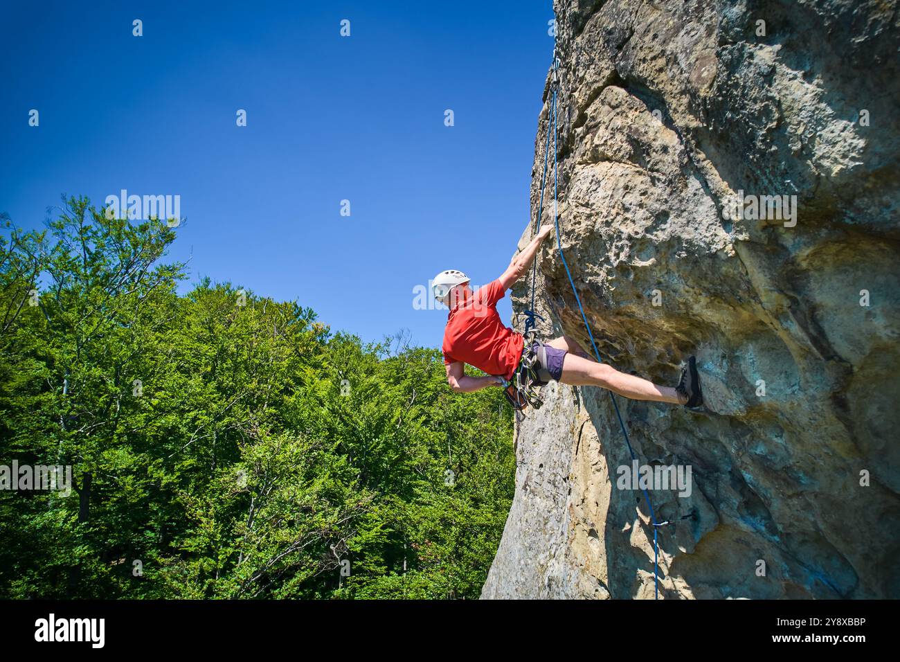 Aerial view of male rock climber ascending rugged limestone cliff with ...