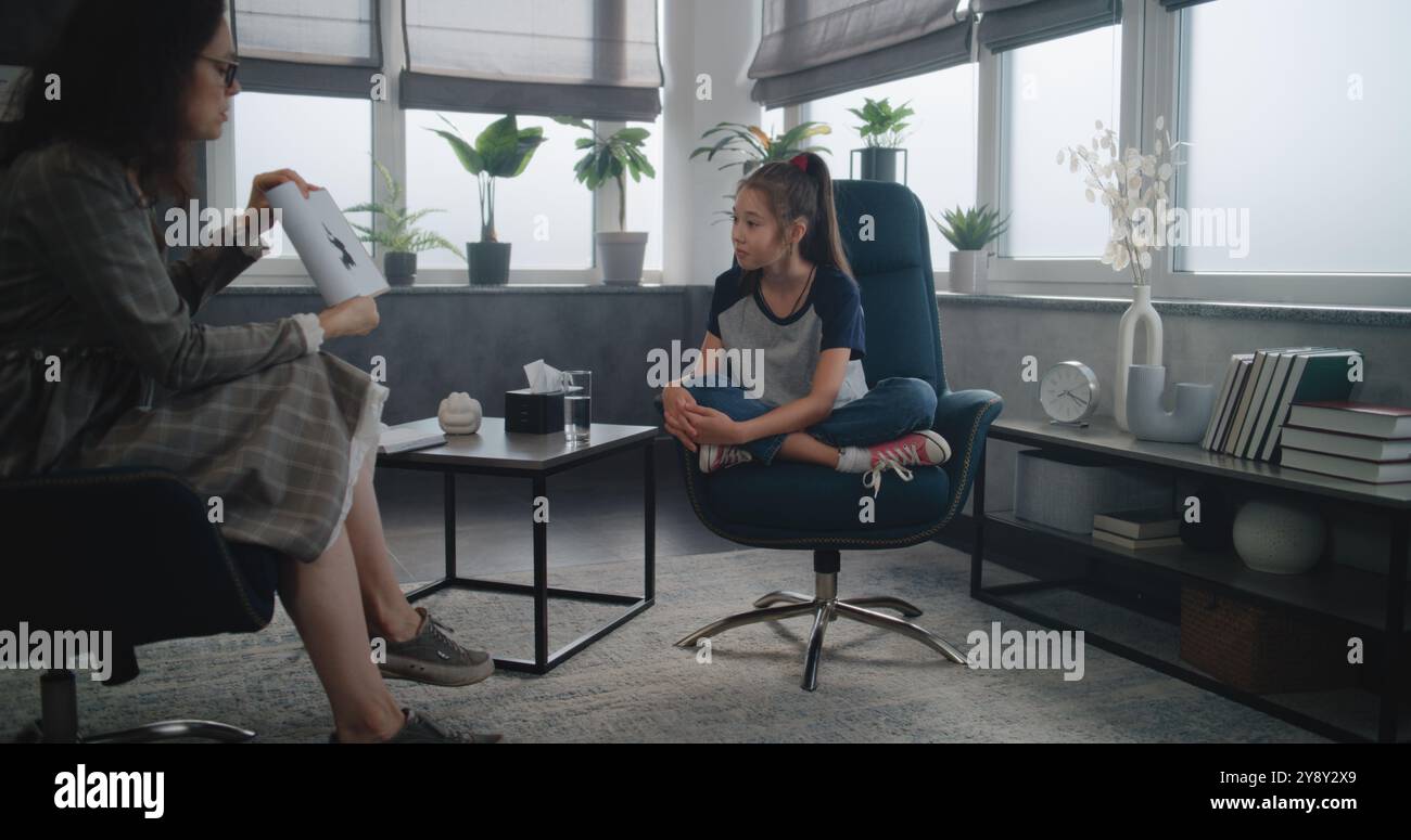 Female child psychologist shows illustrations to Asian school-aged girl ...