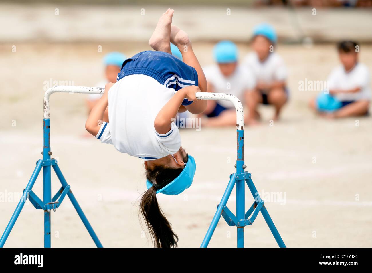 A Japanese girl in P.E. uniform doing gymnastics high bar at a Japanese ...
