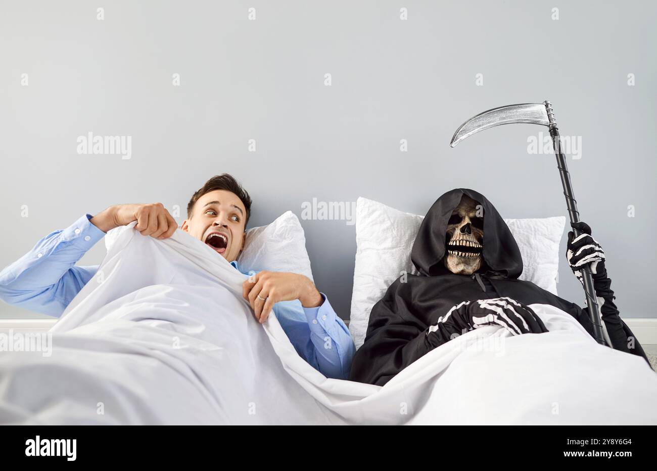 Screaming scared man lying on bed near person in a Halloween grim ...