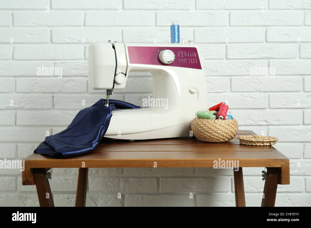 Sewing machine, blue fabric and spools of threads on wooden table near ...