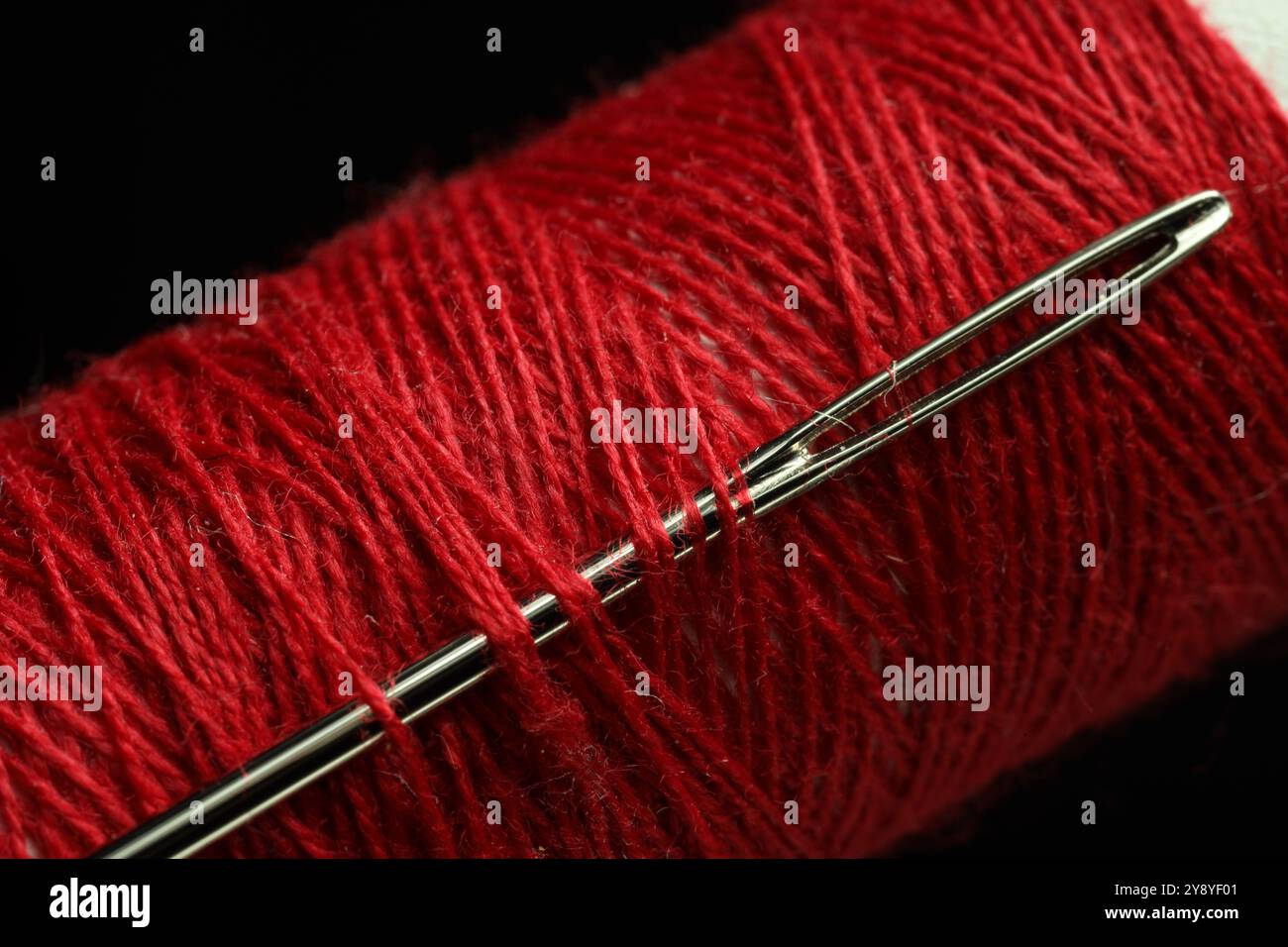 Spool of red sewing thread with needle on black background, closeup ...