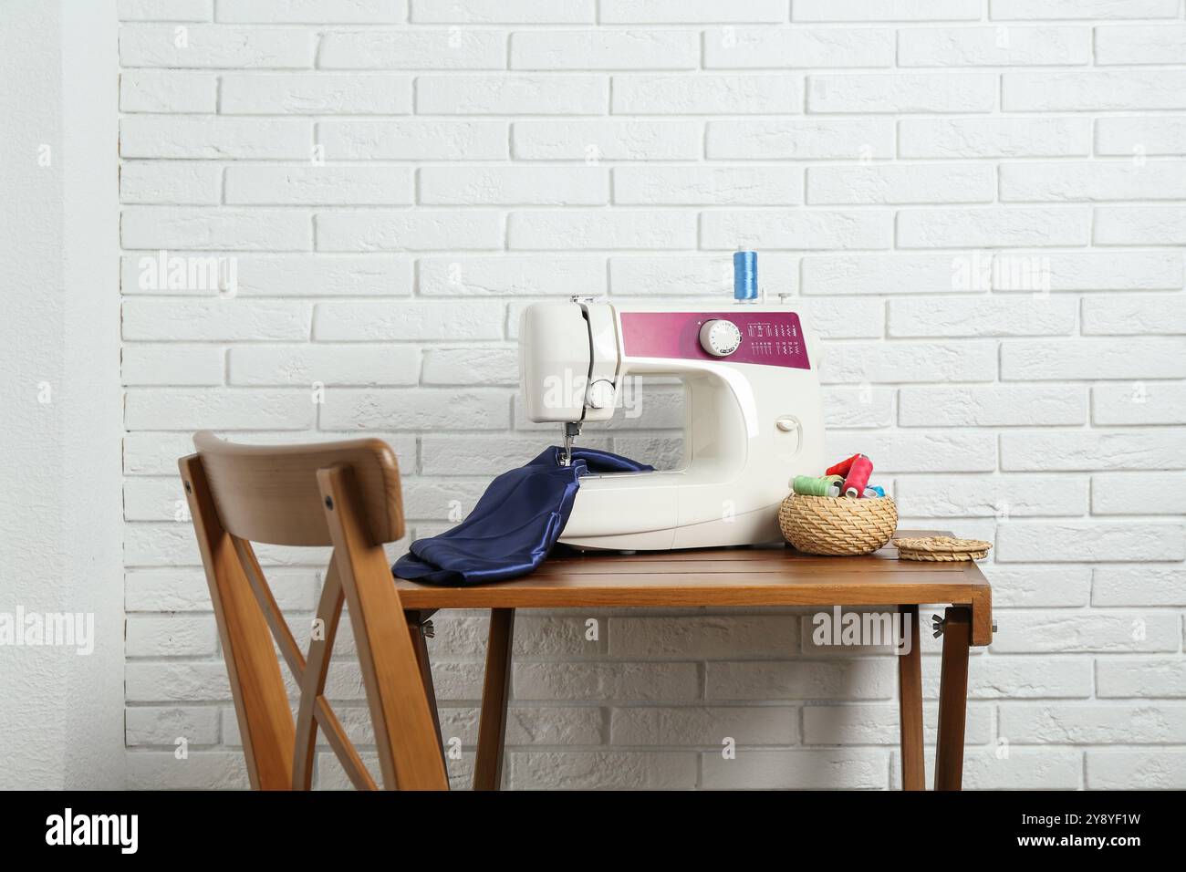 Sewing machine, blue fabric and spools of threads on wooden table near ...