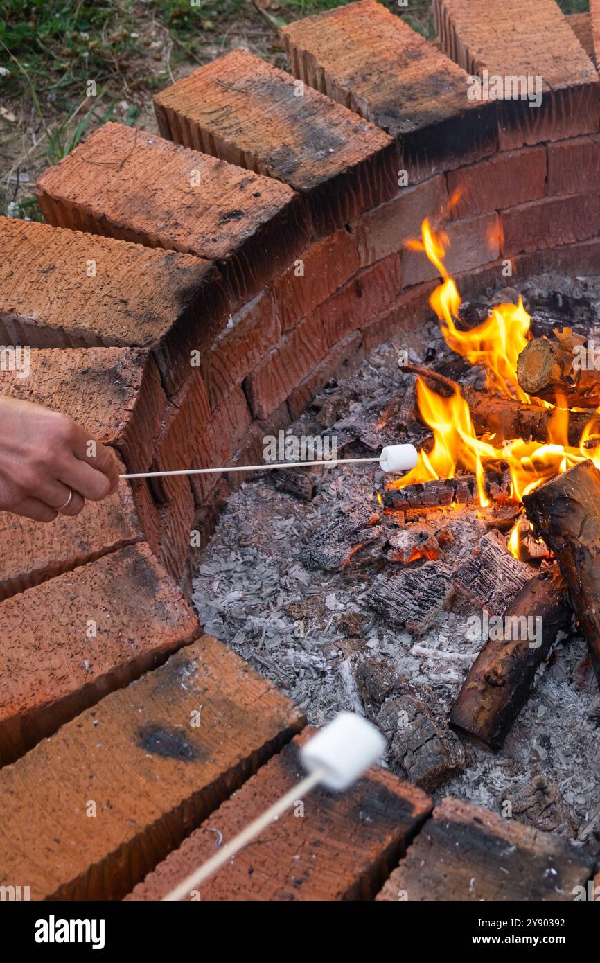 Marshmallows on a skewer are fried over a campfire in round brick fire ...