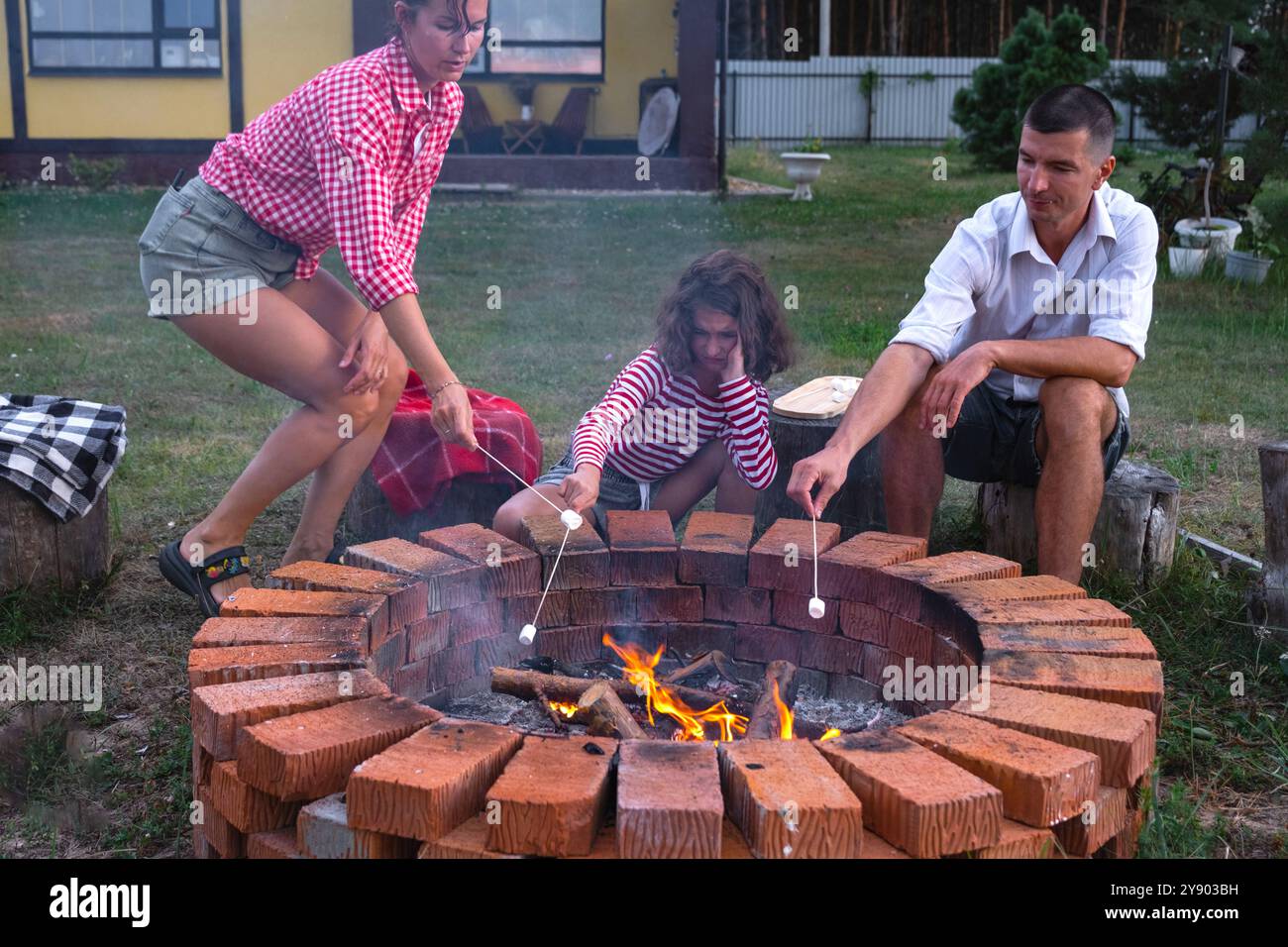 Family mom, dad, daughter roast marshmallows on skewers on a campfire ...