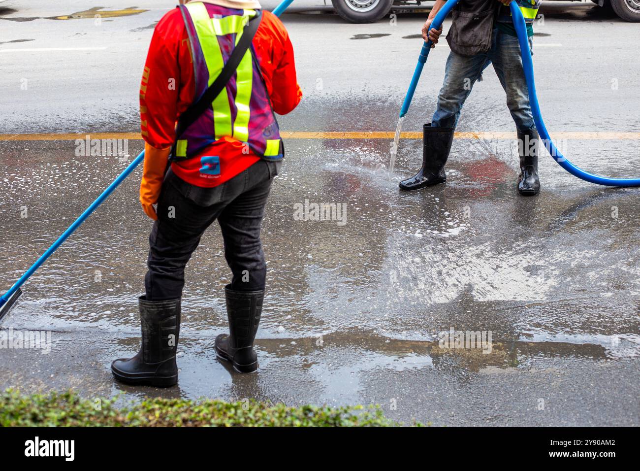 Workers in rubber boots with hoses in their hands wash the road surface ...