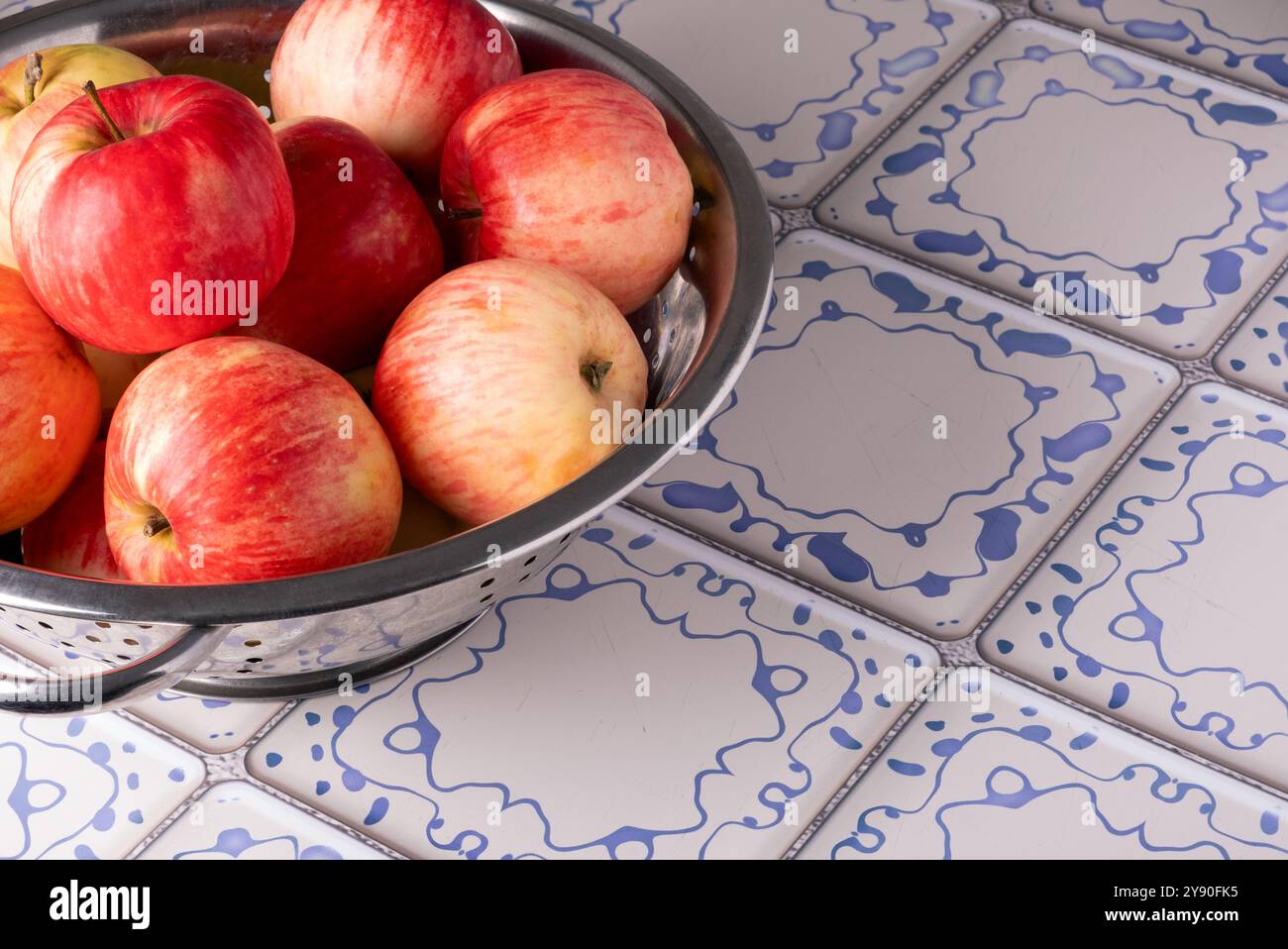 Red apples lie in a metal colander on a table with a blue and white ...