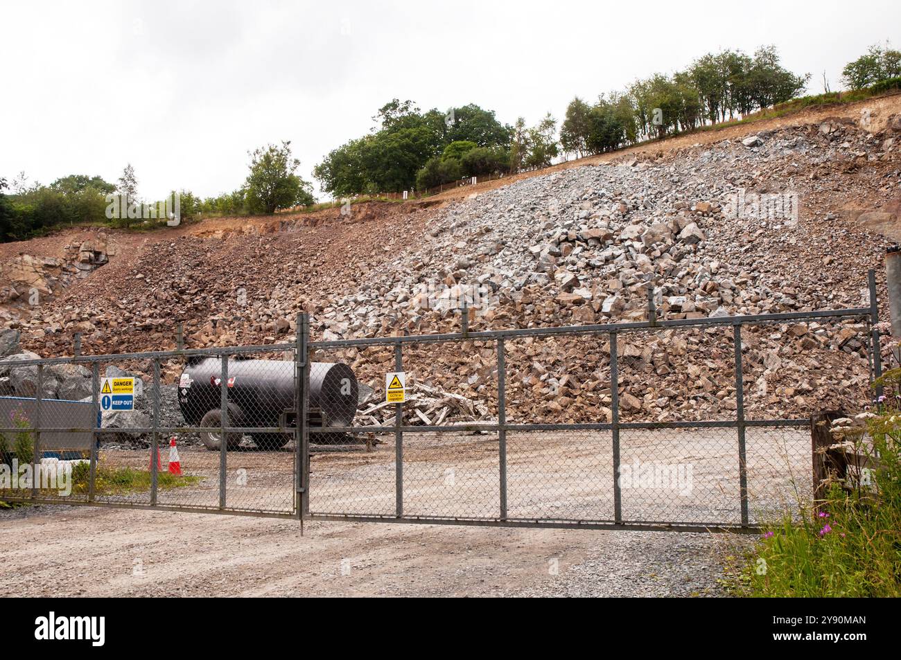 Quarry workings with stone stockpile and security fencing with Danger ...
