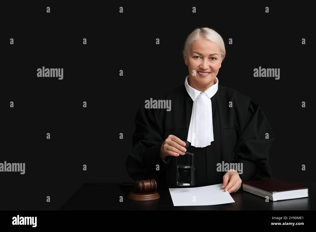 Mature female judge with stamp and document at table on black ...